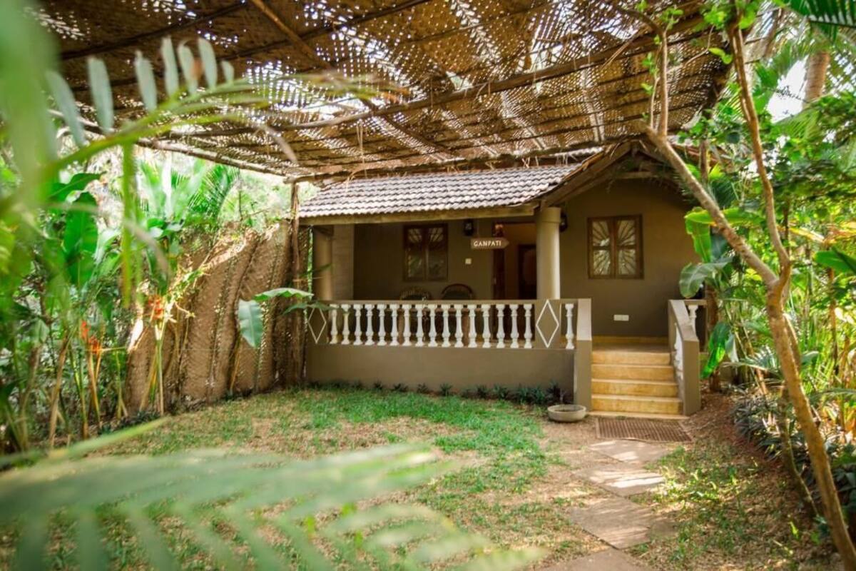 Uma casa com telhado de palha, um pequeno alpendre e uma escadaria que leva à entrada.