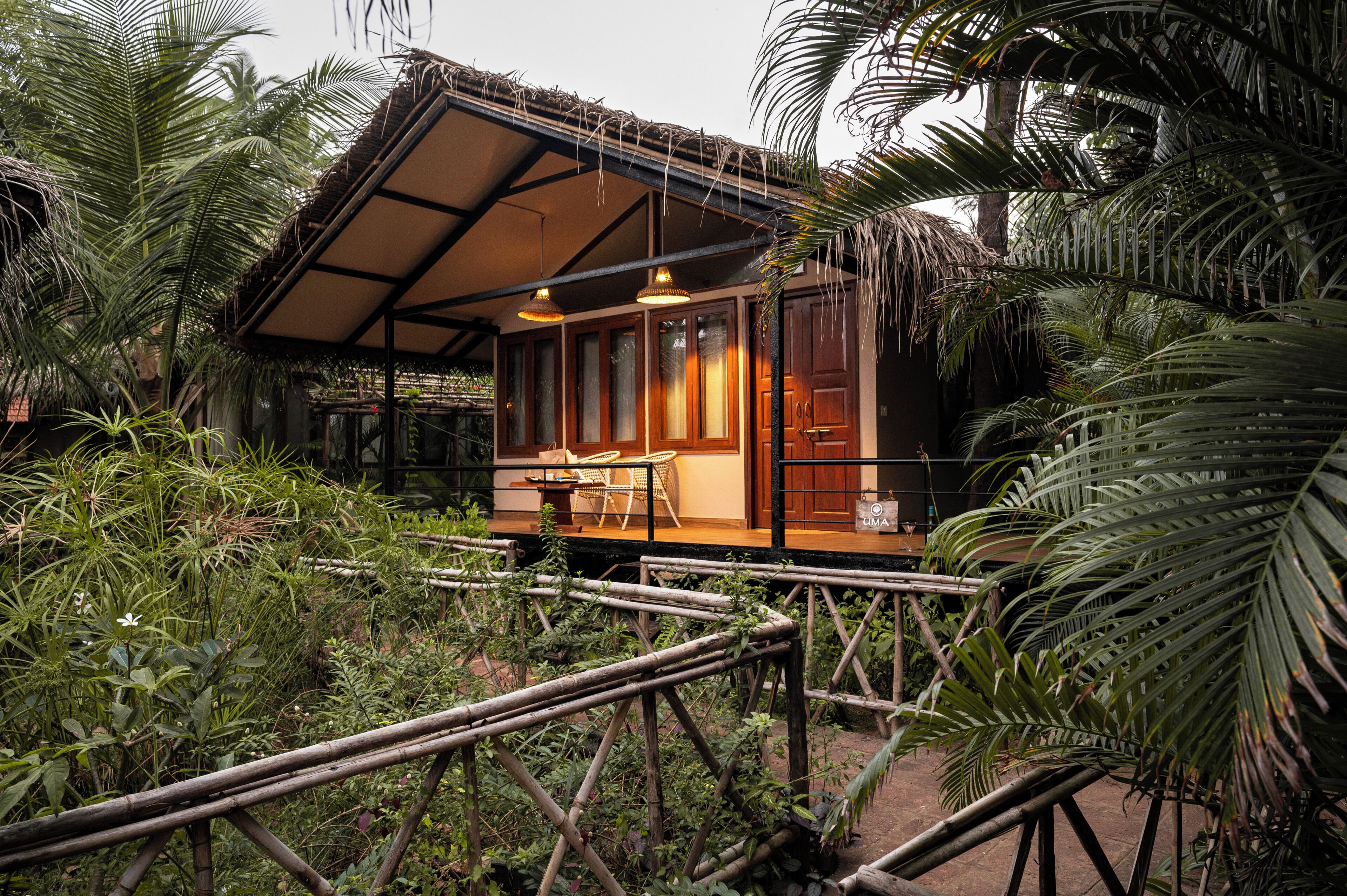 Uma cabana de madeira com telhado de palha, rodeada por vegetação tropical densa.