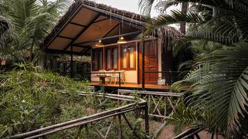Uma cabana de madeira com telhado de palha, rodeada por vegetação tropical densa.