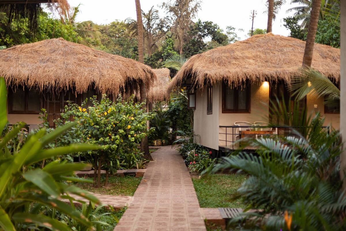 Uma trilha que leva a cabanas com telhado de palha, em meio a vegetação exuberante.