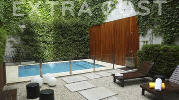 Piscina com deck de madeira, espreguiçadeiras e guarda-corpo de vidro.