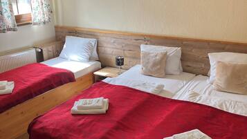 Quarto de hotel com duas camas, cada uma com roupa de cama vermelha e almofadas brancas, uma cabeceira de madeira, uma mesa de cabeceira com abajur e duas fotos emolduradas na parede.