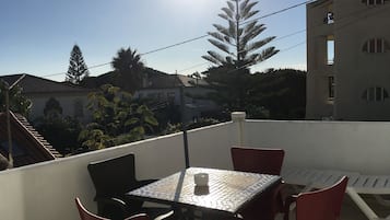 Varanda com mesa e cadeiras, com vista para uma área residencial com árvores e edifícios.
