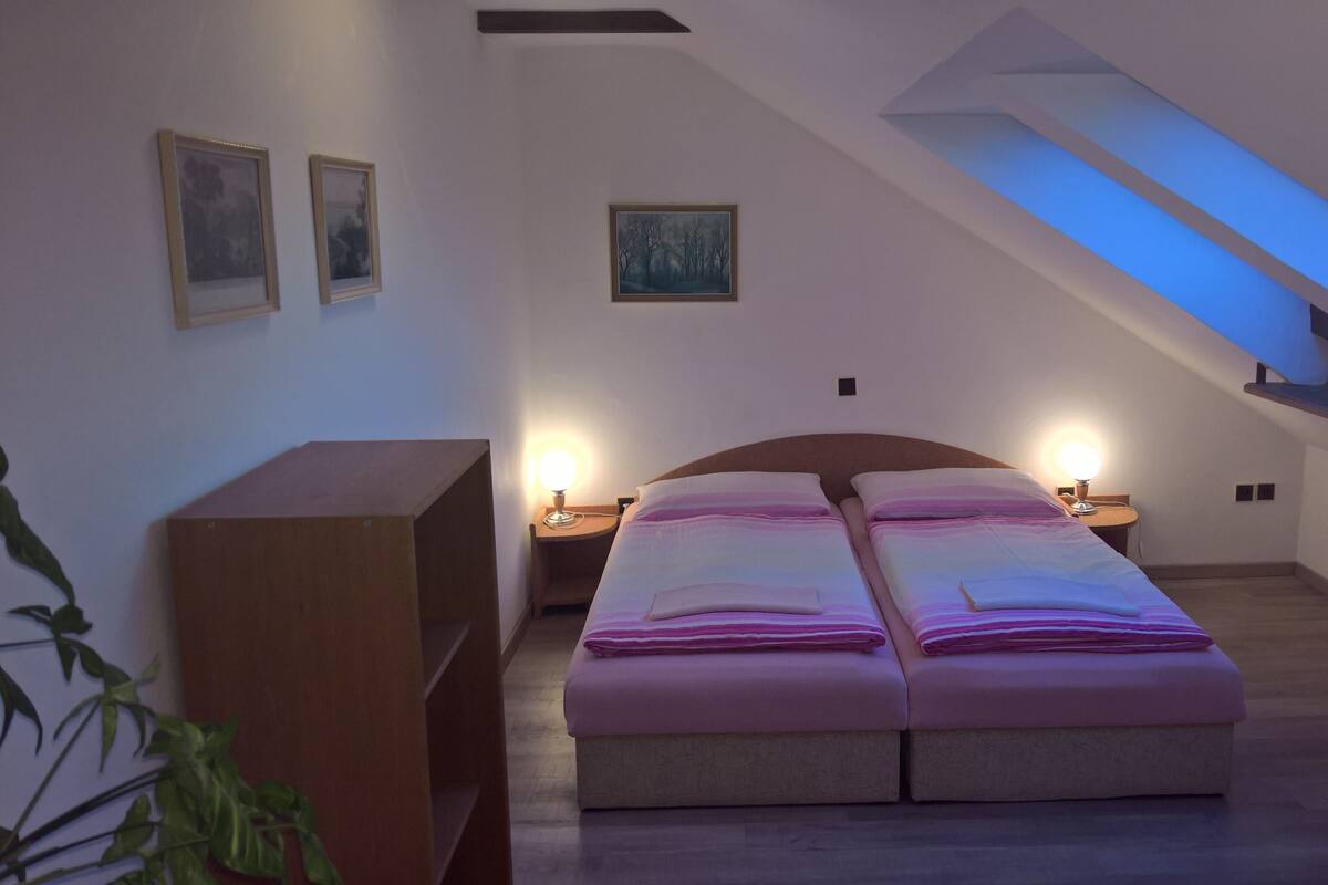 Quarto com uma cama grande, duas mesas de cabeceira com abajures, um banco de madeira e quadros nas paredes.