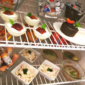 Exposição refrigerada com diversos alimentos, incluindo sobremesas e aperitivos.