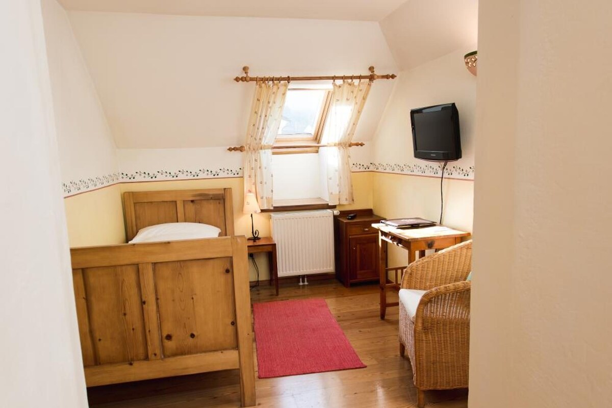 Quarto com cama de madeira, uma mesa pequena, televisão e janela com cortinas.