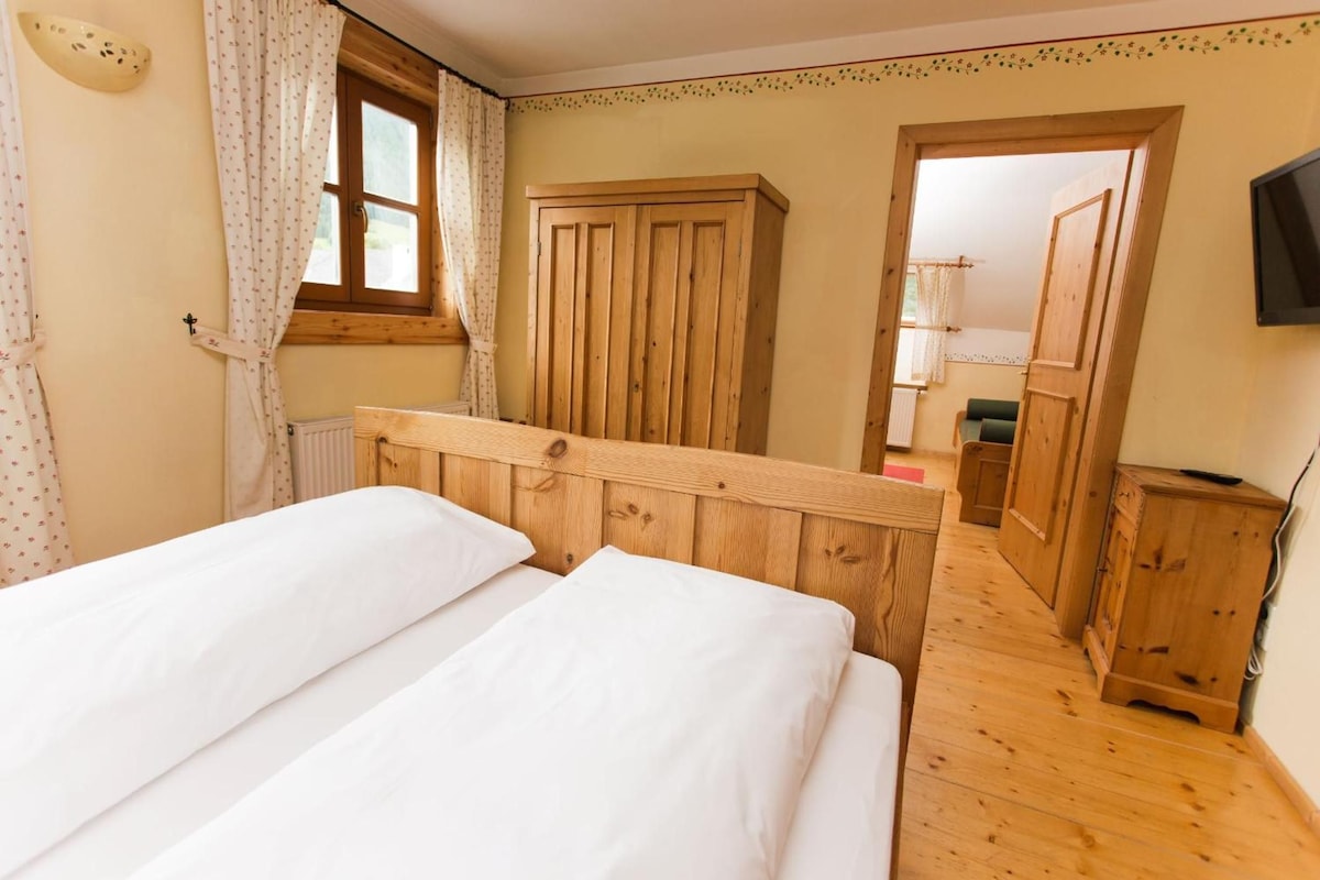 Quarto com cabeceira de madeira, cama com roupa de cama branca, janela com cortinas e guarda-roupa de madeira.