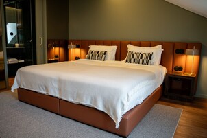 Uma cama grande com cabeceira de madeira, duas luminárias de apoio e um tapete em tons neutros.