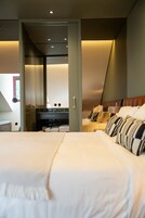 Quarto de hotel moderno com uma cama grande, banheiro com espelho e vista do céu.