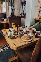 Uma mesa de jantar de madeira com itens de café da manhã, incluindo doces, um pão e um copo de suco de laranja.
