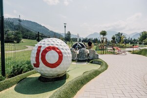 Campo de golfe com uma grande escultura de bola de golfe, área cercada e um caminho pavimentado.