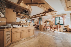Uma cozinha espaçosa com armários de madeira, um espaço de refeições com uma mesa grande e cadeiras, e vista para o exterior através de uma janela.