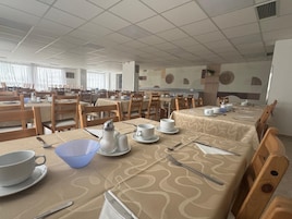 Uma sala de jantar com várias mesas preparadas para o café da manhã, cada uma com pratos, copos e talheres.