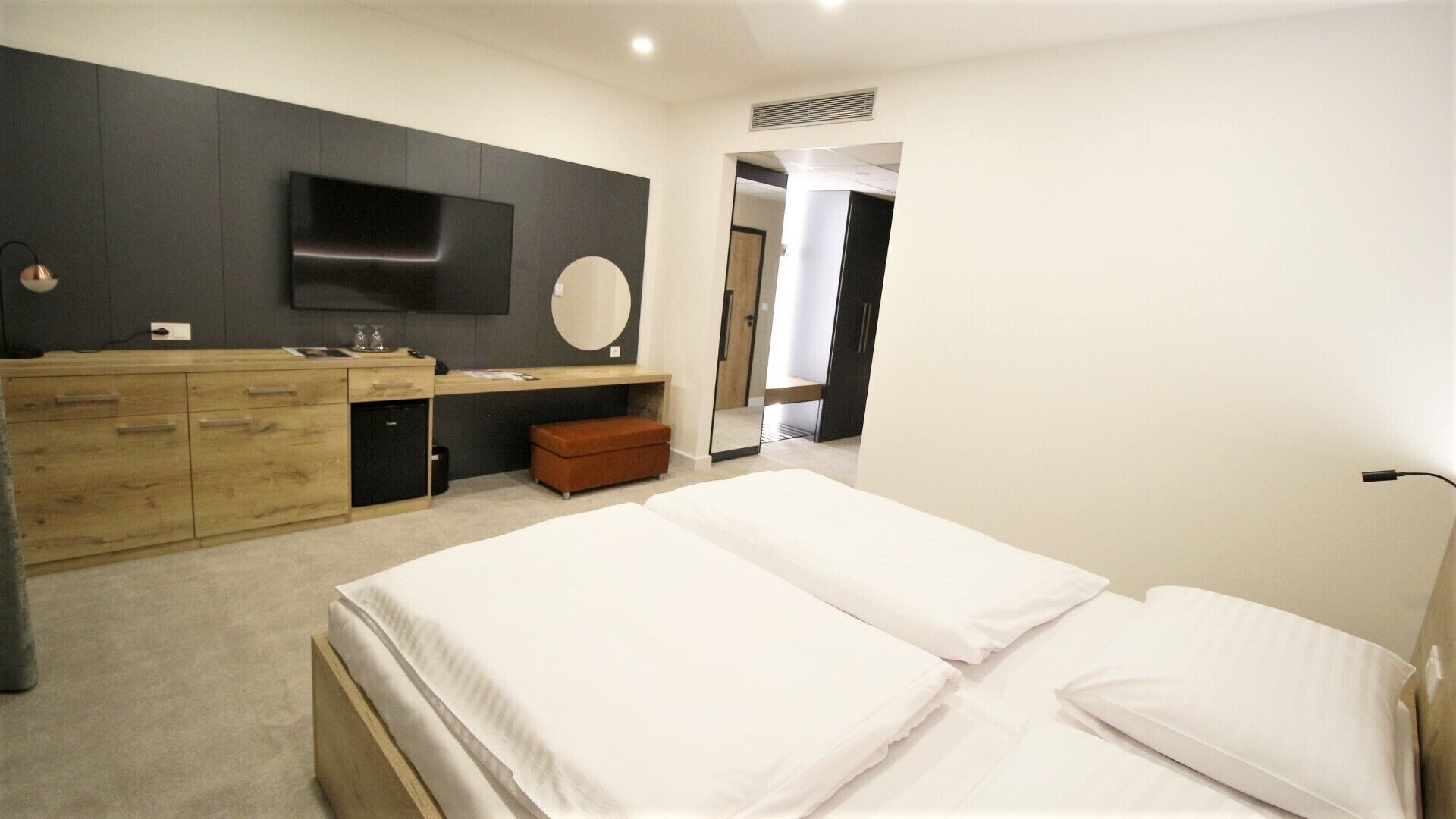 Quarto moderno com cama, escrivaninha, televisão e guarda-roupa.