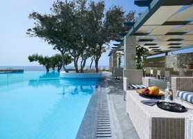 Uma área à beira da piscina com vista desobstruída para o mar, cadeiras de vime e um tabuleiro de frutas.