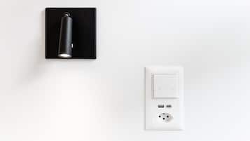 Uma luminária preta fixada na parede e uma tomada branca com tomadas USB e para energia.