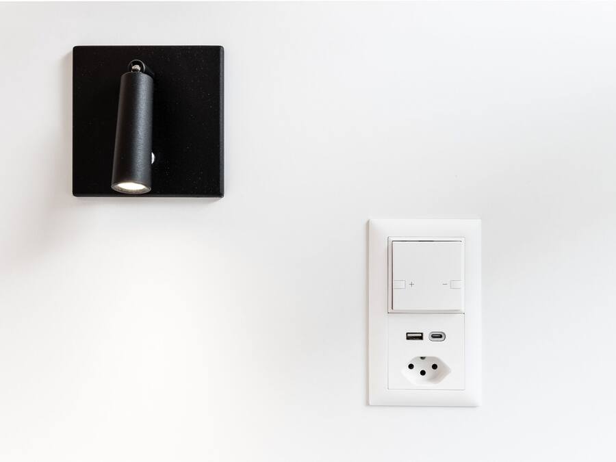 Uma luminária preta fixada na parede e uma tomada branca com tomadas USB e para energia.