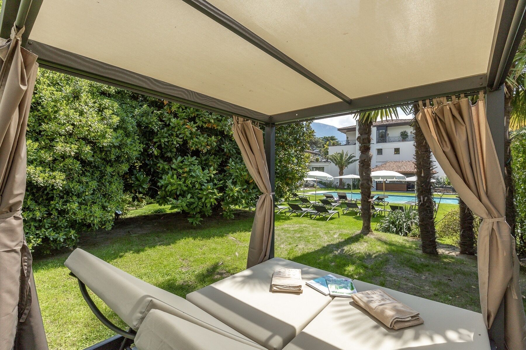 Uma área de estar coberta ao ar livre, com vista para uma piscina e vegetação.