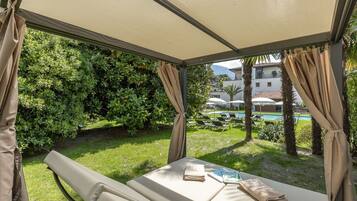 Uma área de estar coberta ao ar livre, com vista para uma piscina e vegetação.