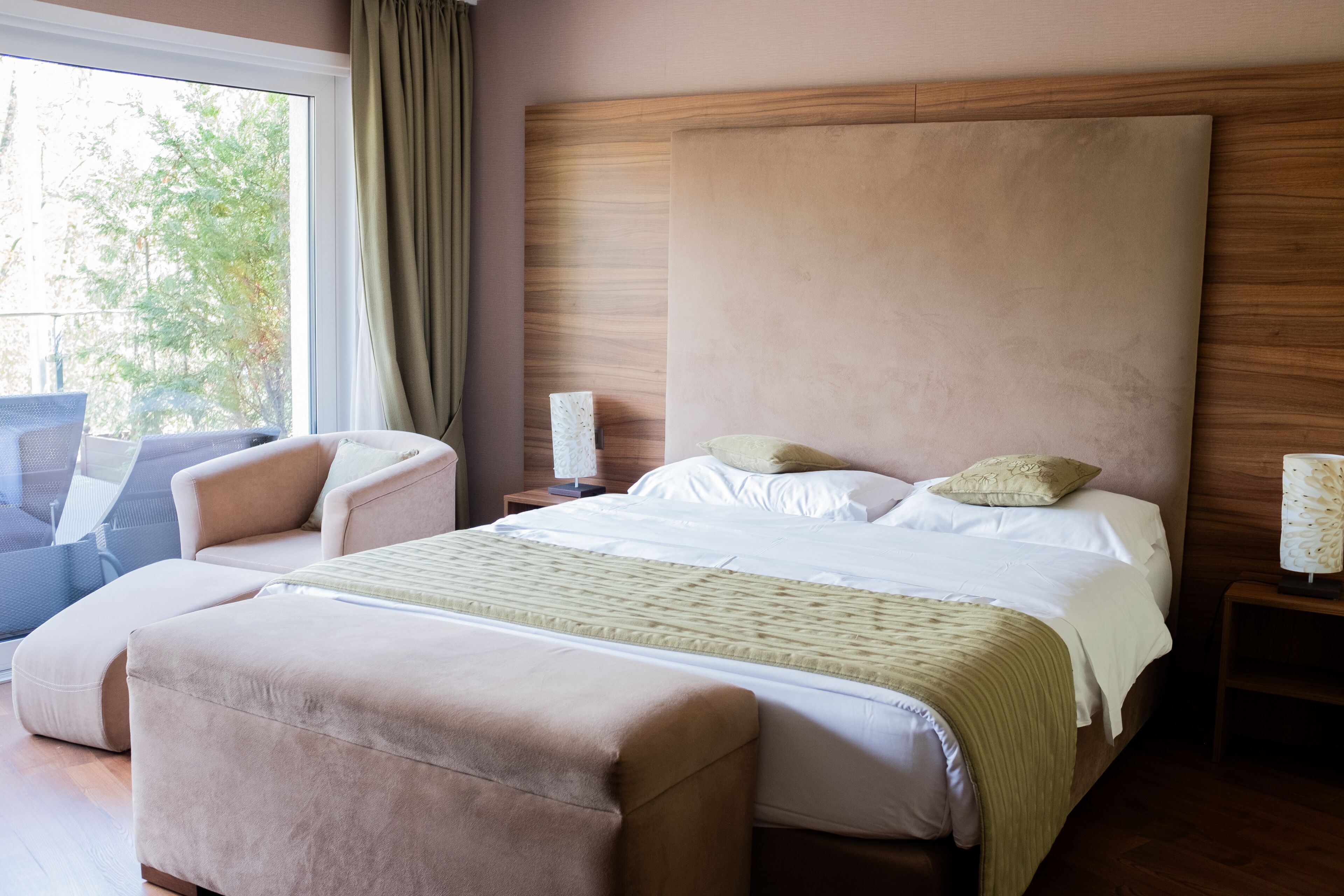 Quarto de hotel moderno com uma cama grande, um sofá, uma mesa de cabeceira e uma janela com cortinas.