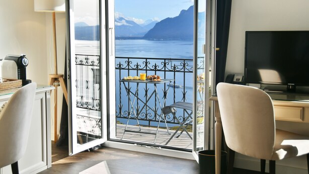 Quarto com vista para um lago e montanhas, uma mesa de jantar com comida e bebidas, uma televisão e uma cadeira.