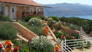 Uma casa com telhado de telhas vermelhas, varanda e um jardim com diversas flores.