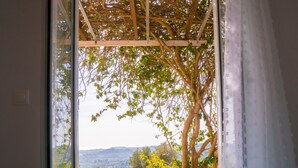Quarto com cama, vista para árvores e colinas através de uma janela, e uma estrutura de pérgola de madeira.