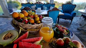 Disposição para o pequeno-almoço com uma cesta de frutas, fatias de melancia, um jarro de sumo de laranja e uma romã sobre uma mesa.