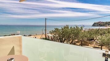 Uma varanda com vista para o mar, uma mesa com uma cadeira e um pequeno edifício com uma bandeira.