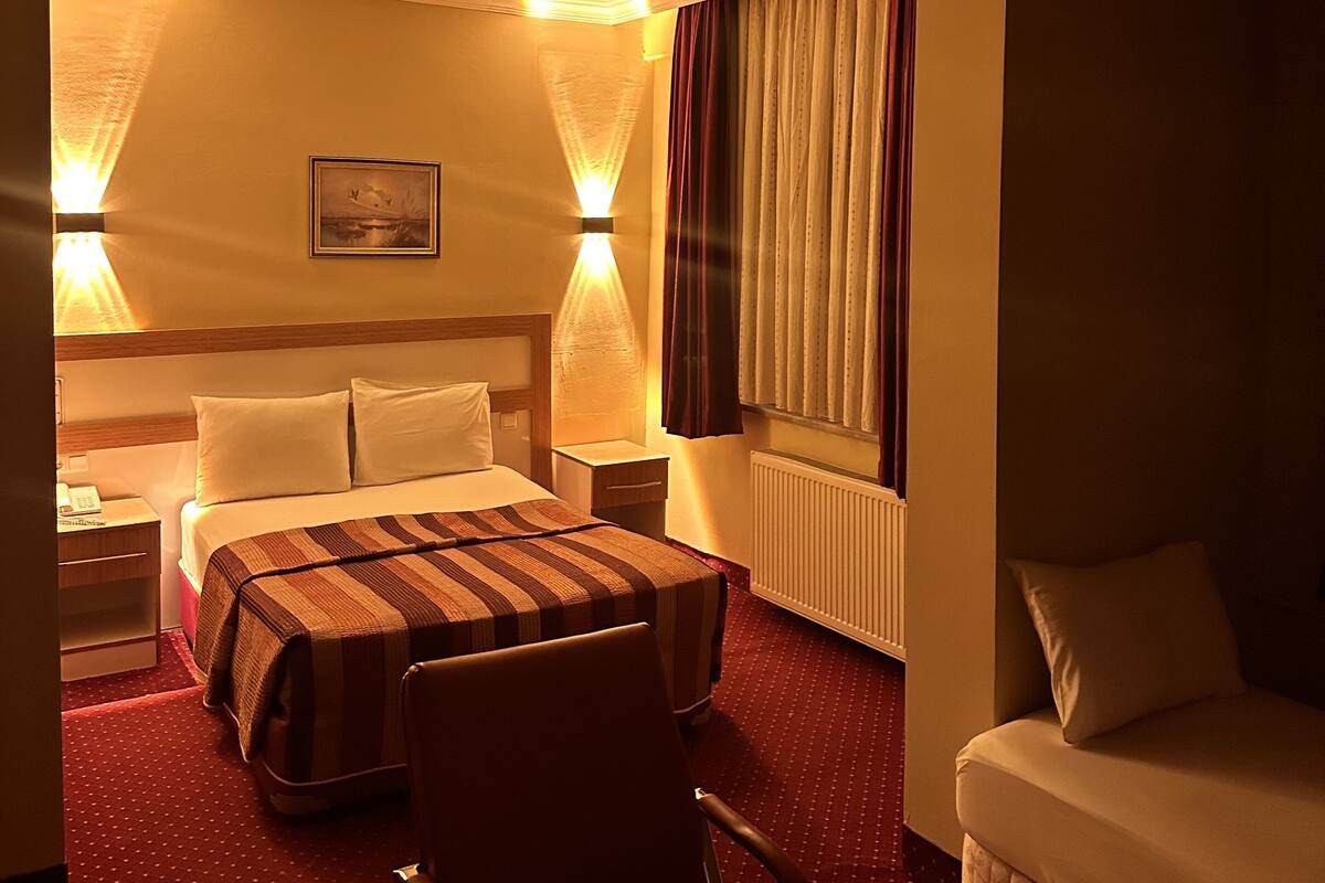 Quarto de hotel com cama, cadeira, mesa, mesa de cabeceira e janela com cortinas.