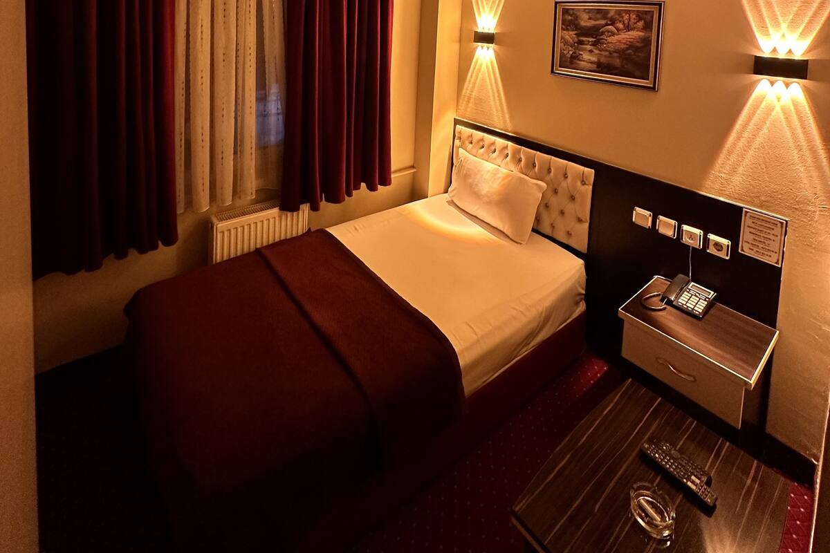 Quarto de hotel com uma cama, mesa de cabeceira com abajur, telefone e um quadro na parede.