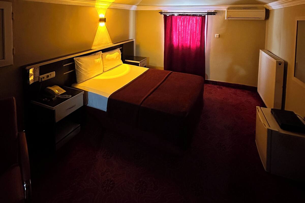Quarto de hotel com cama, mesa de cabeceira, abajur e radiador.