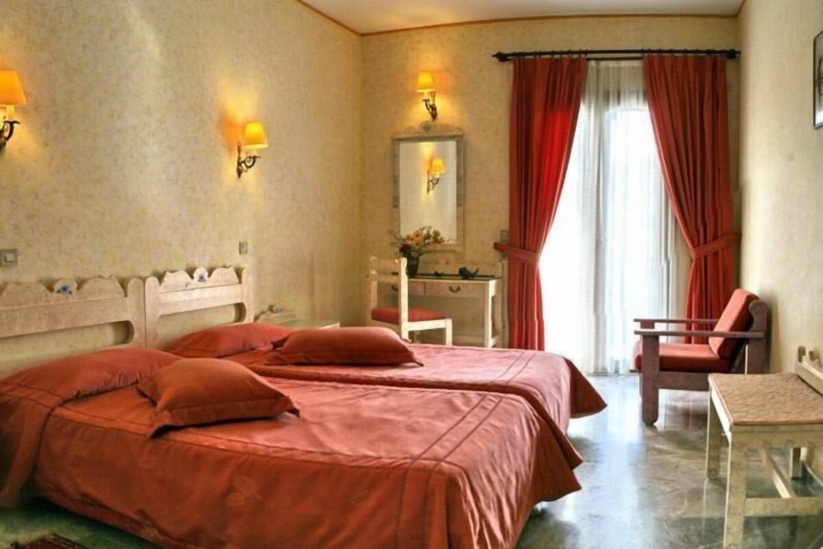 Quarto de hotel com duas camas, uma escrivaninha, uma cadeira e um espelho.
