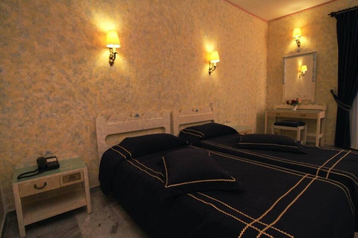 Quarto de hotel com cama de casal, duas mesas de cabeceira, um criado-mudo, espelho e arandelas.