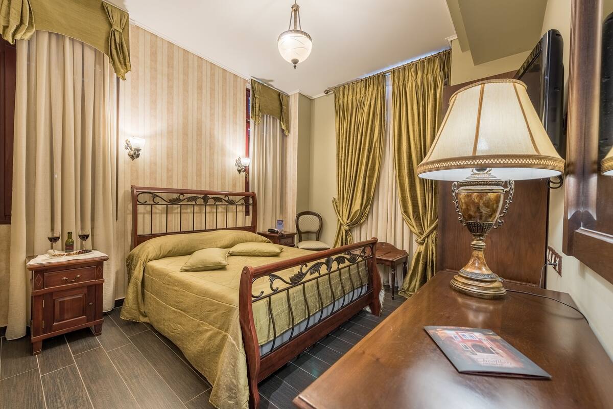 Quarto de hotel com cama, mesa de cabeceira, abajur e cortinas.