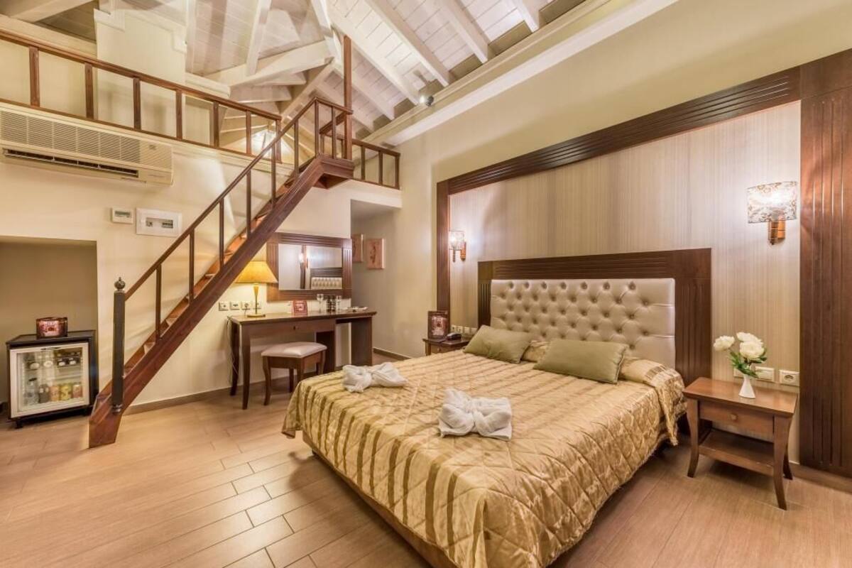 Quarto com uma cama grande, escrivaninha, cadeira, escada e um minibar.
