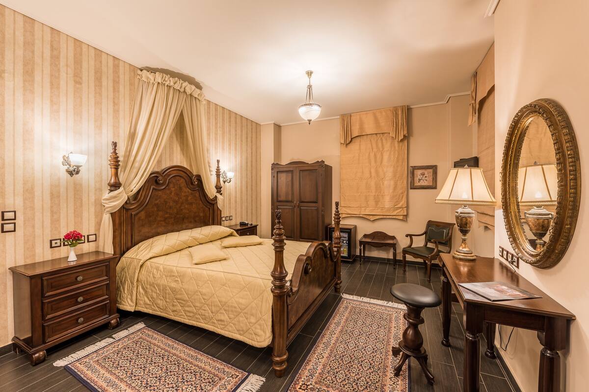 Quarto com cama de dossel, mesa de cabeceira, cômoda, escrivaninha, cadeira, espelho e tapete.