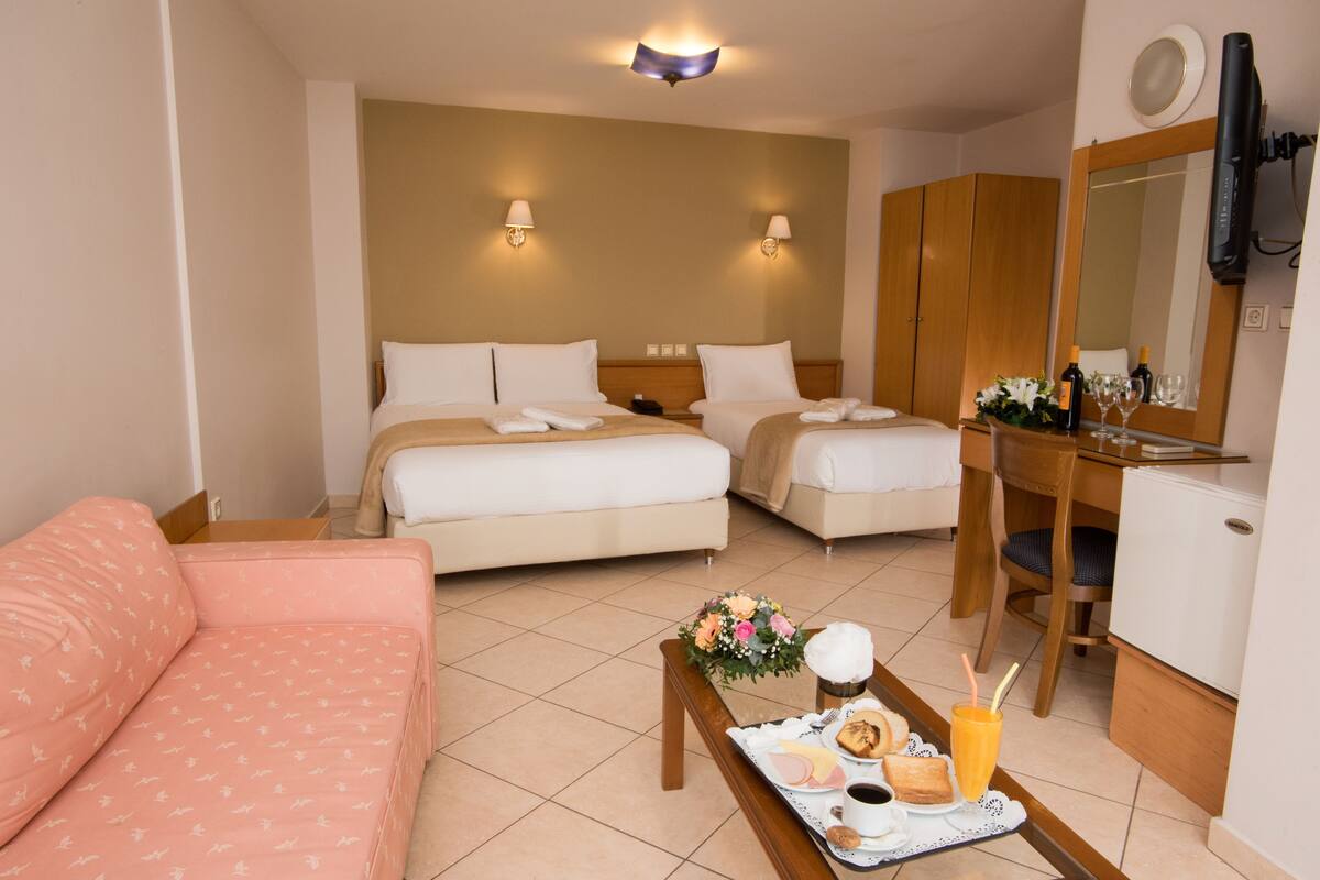 Quarto de hotel com duas camas, um sofá, uma mesa de trabalho e um serviço de café da manhã.