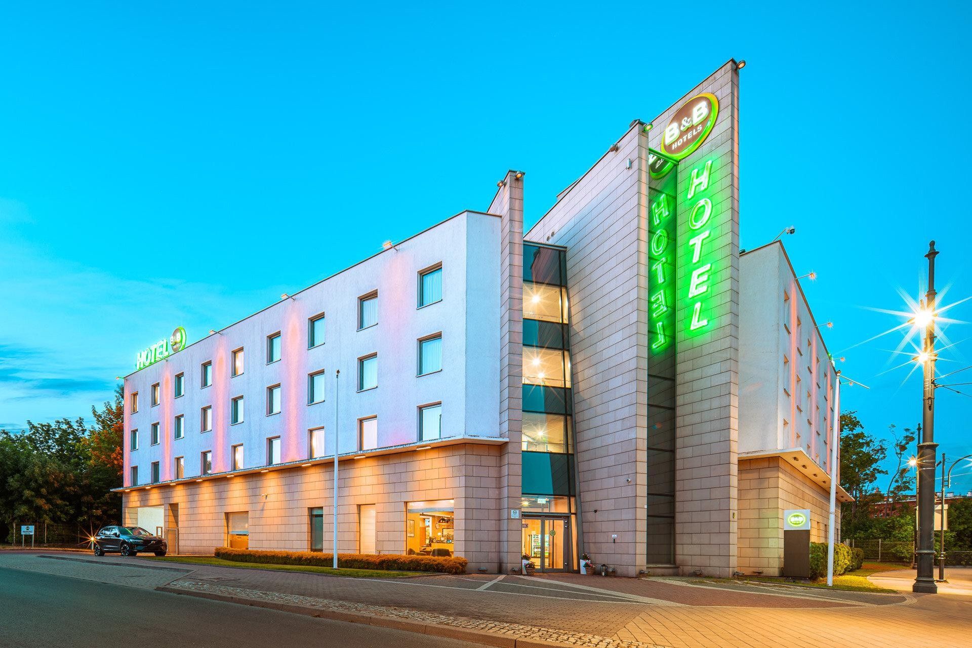 Hotel com fachada moderna, diversas janelas e um letreiro de neon chamativo.