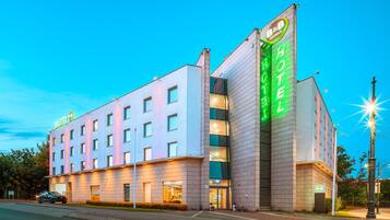 Hotel com fachada moderna, diversas janelas e um letreiro de neon chamativo.