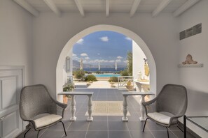 Vista de varanda com arco branco, sobre um piscina e área externa com cadeiras de vime e uma mesa.