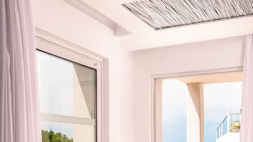 Quarto de hotel com uma cama grande, porta de vidro deslizante para uma varanda com mobiliário de exterior e vista para o mar.