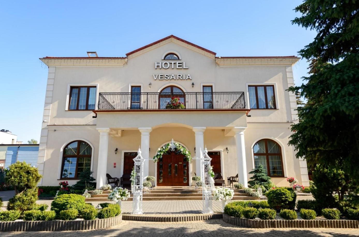 Um hotel de dois andares com entrada imponente, janelas em arco e varanda com grades.