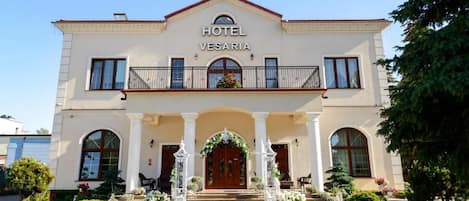 Um hotel de dois andares com entrada imponente, janelas em arco e varanda com grades.