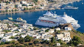 Um grande navio de cruzeiro atracado em um porto com edifícios brancos e uma paisagem montanhosa ao fundo.