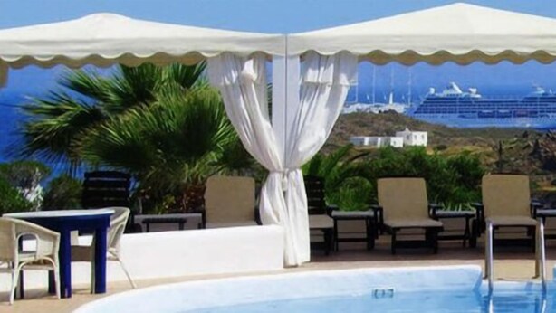 Área de piscina com toldos brancos, cadeiras de sol e uma vista de um navio de cruzeiro ao fundo.
