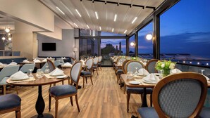Restaurante moderno com piso de madeira, mesas redondas e cadeiras azuis com almofadas.