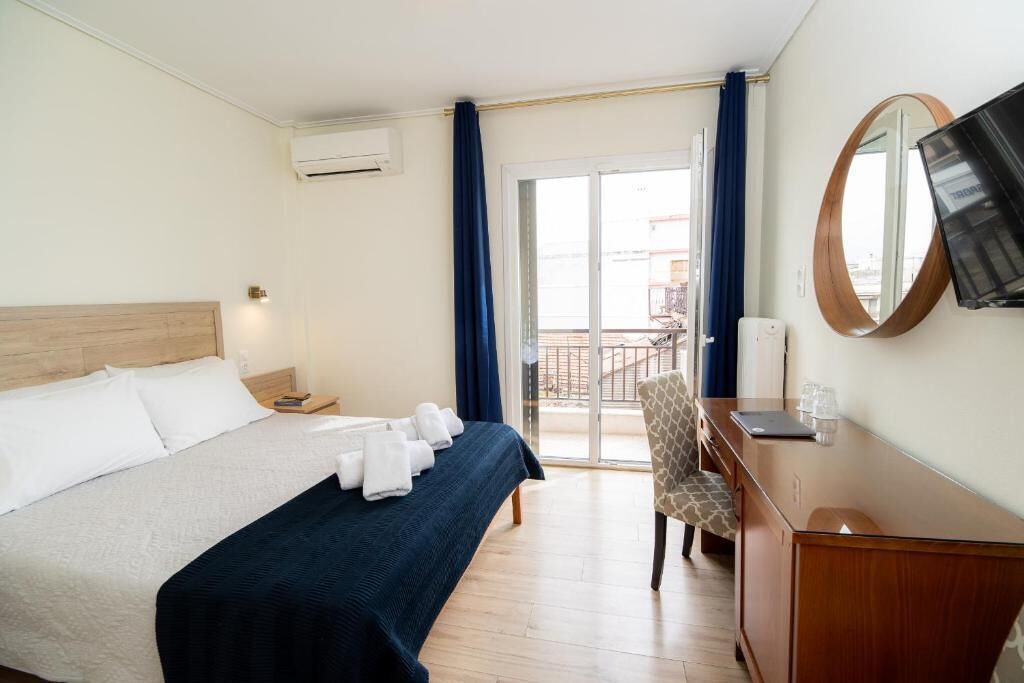 Quarto de hotel com cama, escrivaninha, cadeira, televisão e varanda com vista.