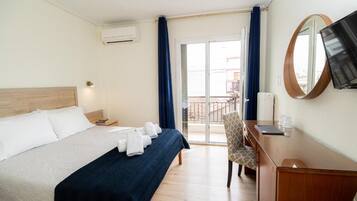 Quarto de hotel com cama, escrivaninha, cadeira, televisão e varanda com vista.