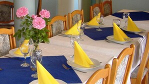 Uma área de refeições com mesas preparadas para vários convidados, cada uma com uma folha amarela, uma taça de vinho e um prato.